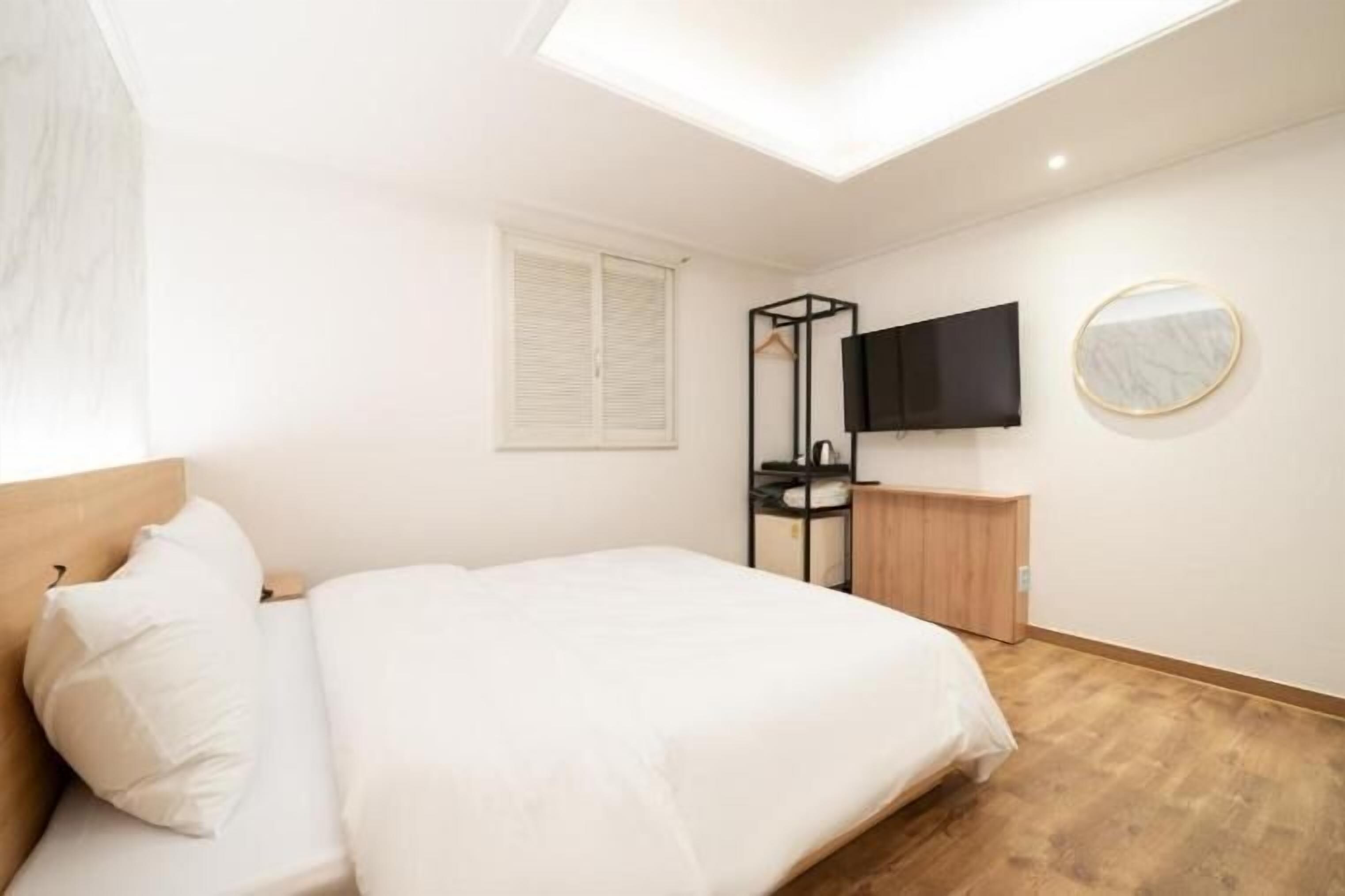 Quarto com cama, televisão na parede, guarda-roupa e claraboia.