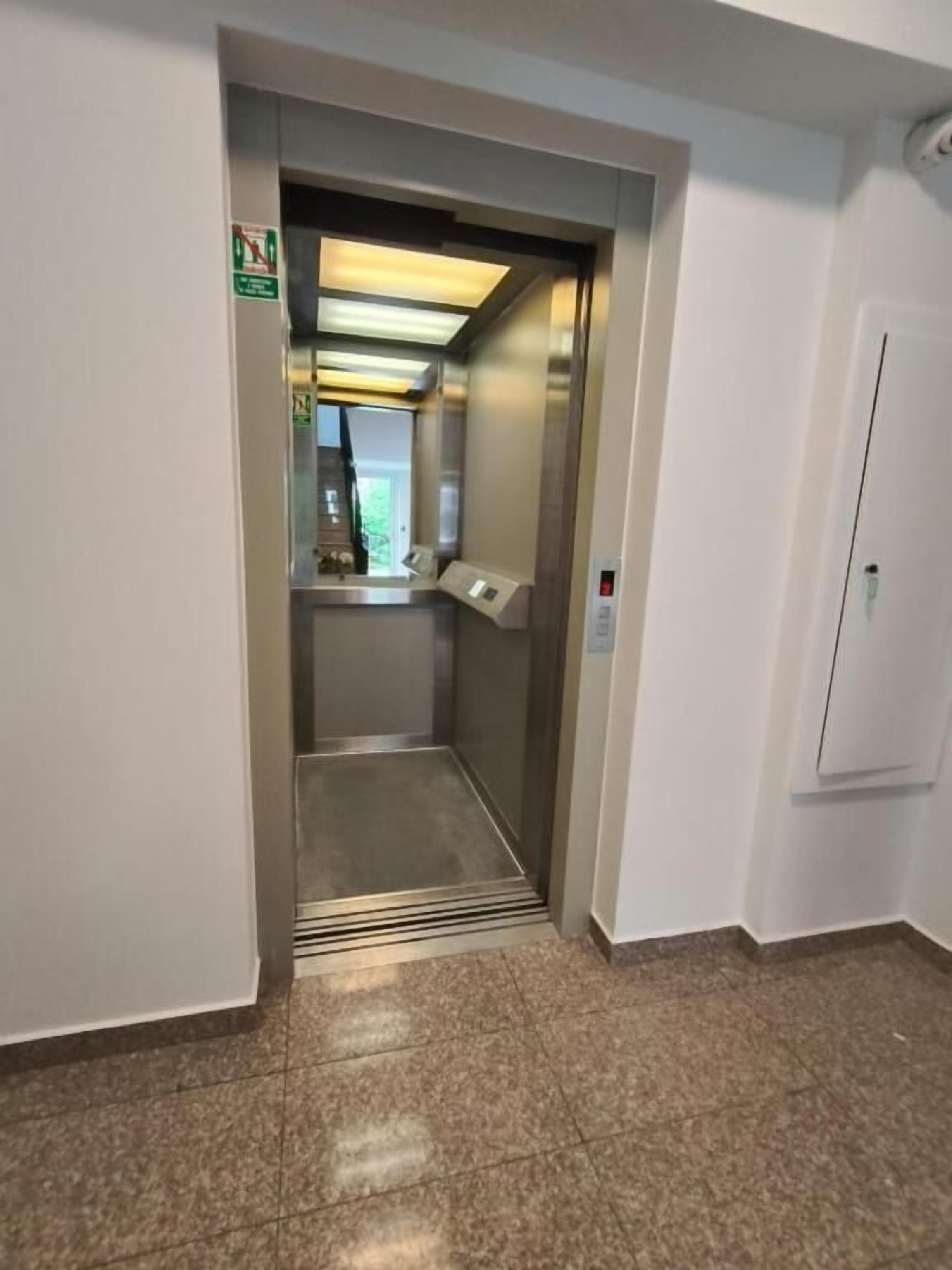 Um elevador com interior metálico, um painel de controle e uma porta com puxador.