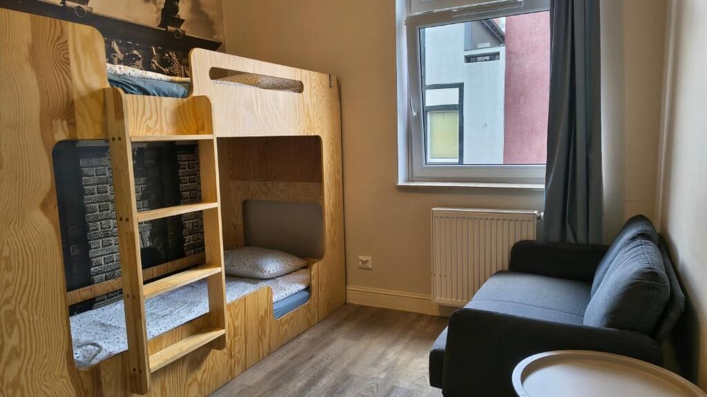 Quarto com uma cama beliche, um sofá e uma janela com vista para um edifício.