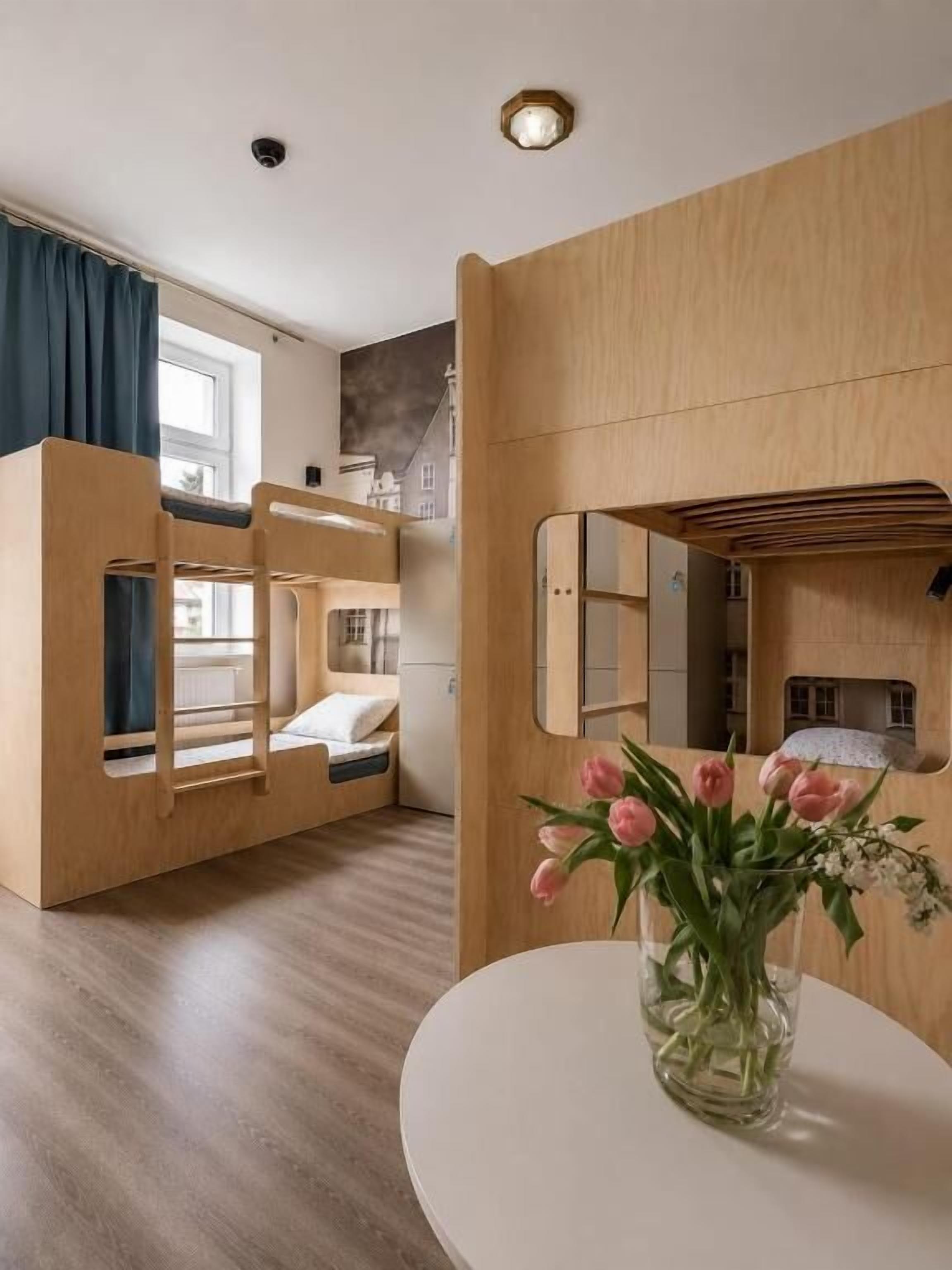 Quarto com beliches, uma mesa redonda com um vaso e um espelho.