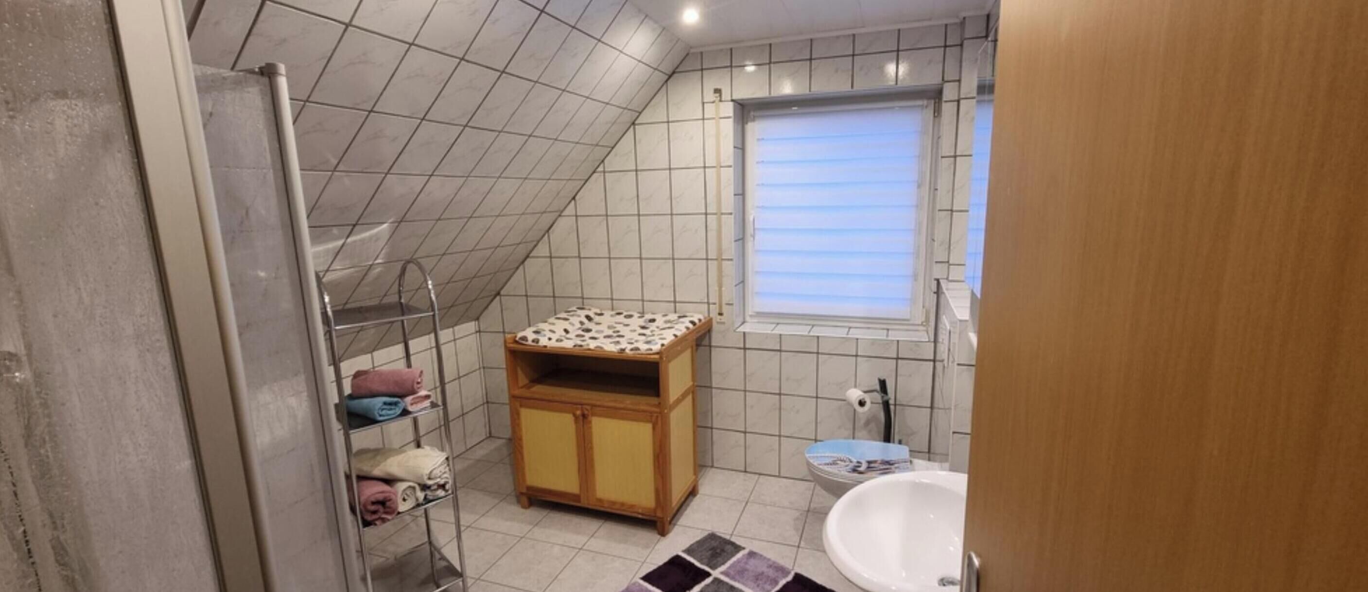 Um banheiro pequeno, com azulejos, um chuveiro, um armário de madeira e um vaso sanitário.