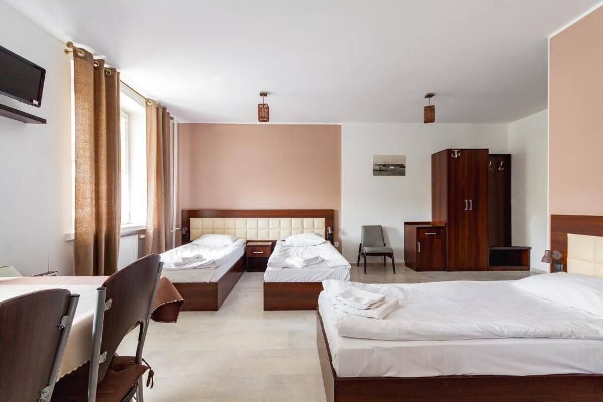 Quarto de hotel com duas camas, uma escrivaninha, uma cadeira, um guarda-roupa e uma televisão.