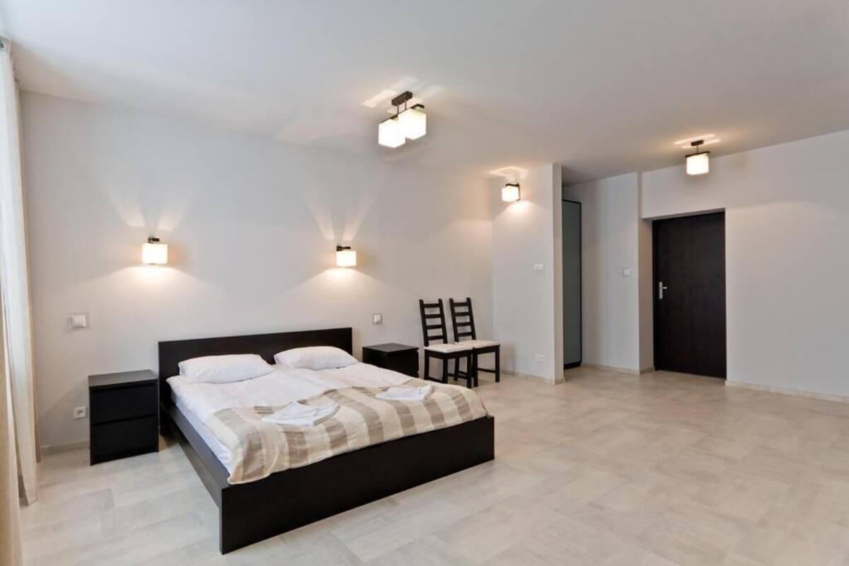 Quarto com cama, mesas de cabeceira, uma cadeira e luminárias na parede.