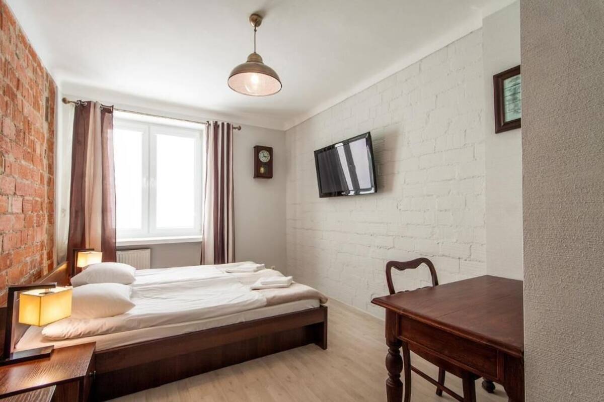Quarto com uma cama, uma escrivaninha, uma cadeira, televisão e janela com cortinas.