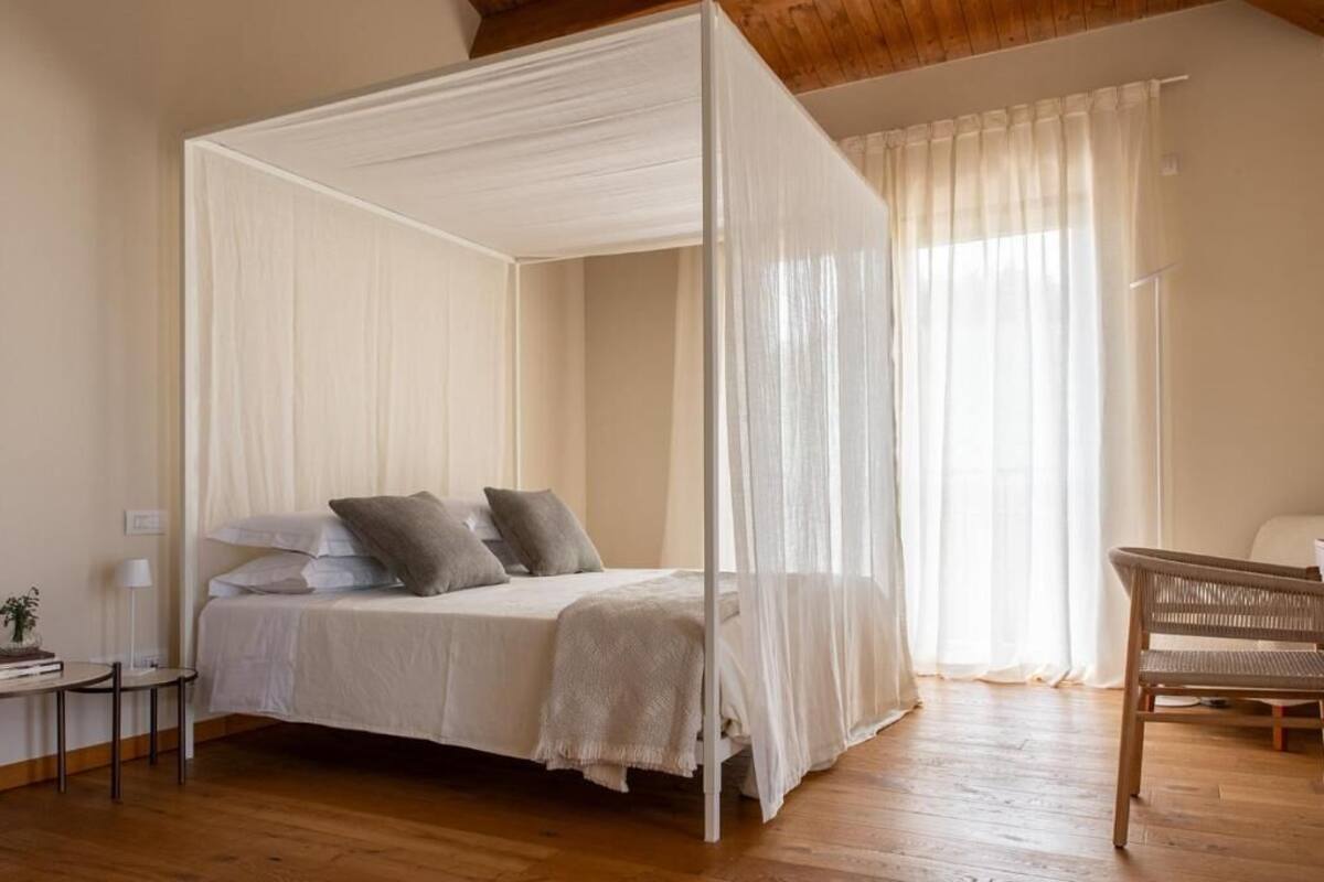 Quarto com uma cama de dossel, uma mesinha com abajur e uma cadeira.