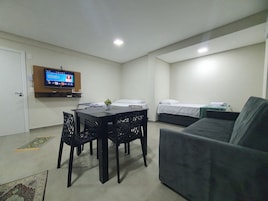 Um quarto com mesa de jantar, cadeiras, sofá, televisão fixada na parede e uma cama.