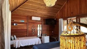 Quarto de cabana de madeira com duas camas, um ventilador de teto, televisão e um lustre rústico.