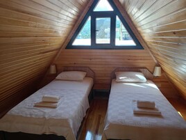 Quarto de sótão acolhedor com duas camas, paredes de madeira e uma janela triangular.