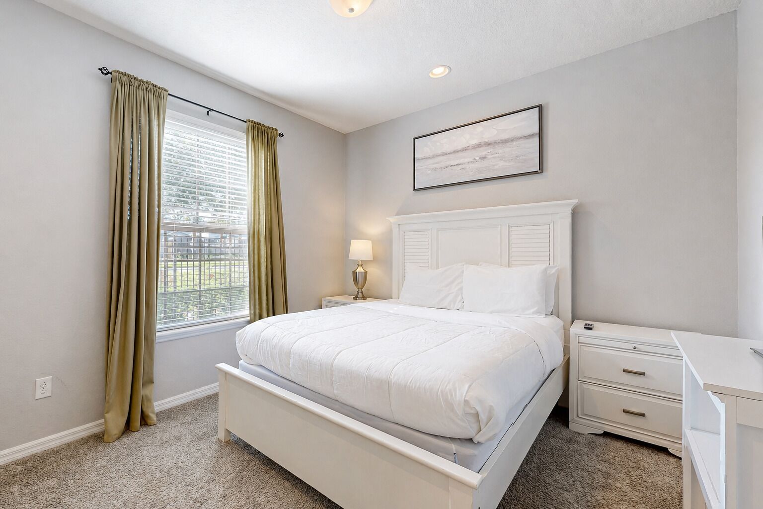 Quarto com cama, mesa de cabeceira, abajur e janela com cortinas.
