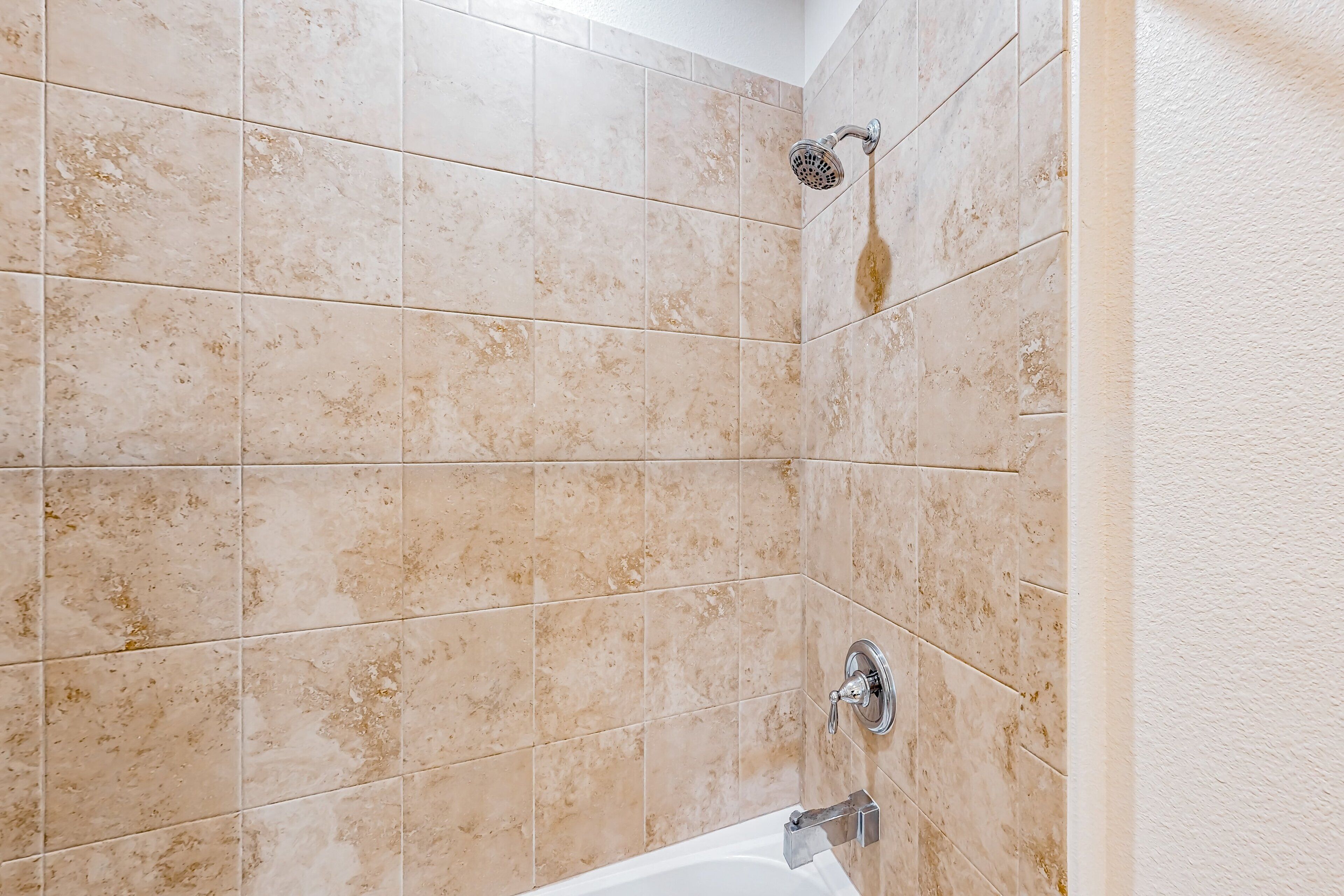 Casa de banho com azulejos bege, um chuveiro e uma torneira de banheira.