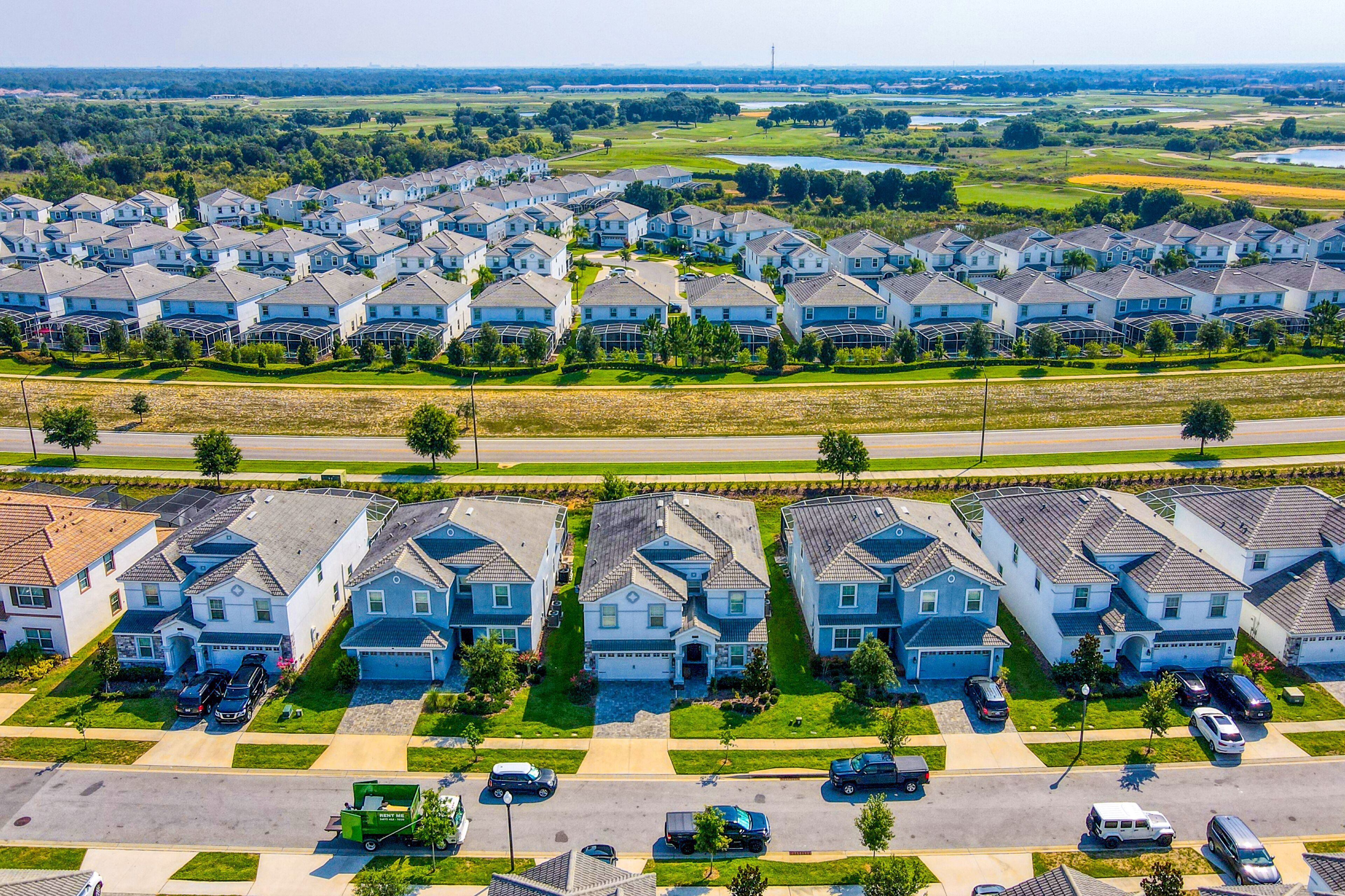 Zona residencial com várias casas de dois andares, uma rua principal e um campo de golfe ao fundo.
