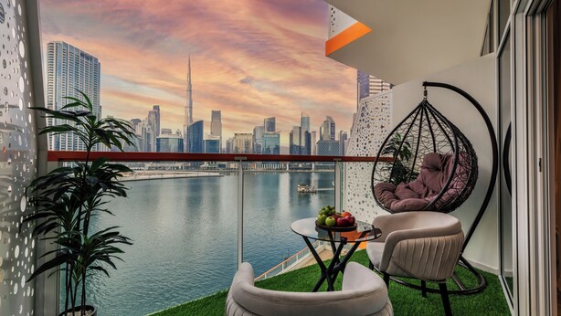Uma varanda com vista para a cidade, uma cadeira suspensa, uma mesinha com frutas e um vaso de planta.