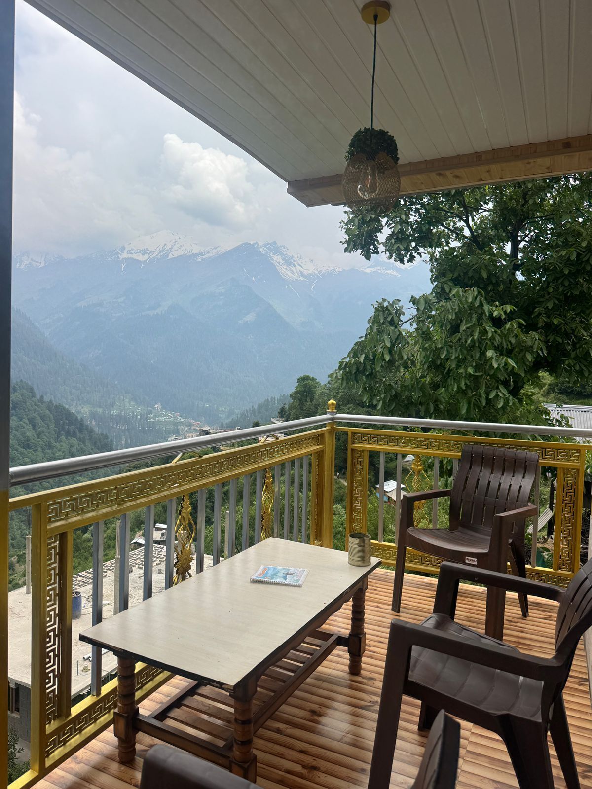 Uma varanda com mesa e cadeiras, uma planta pendurada e vista para montanhas cobertas de neve.