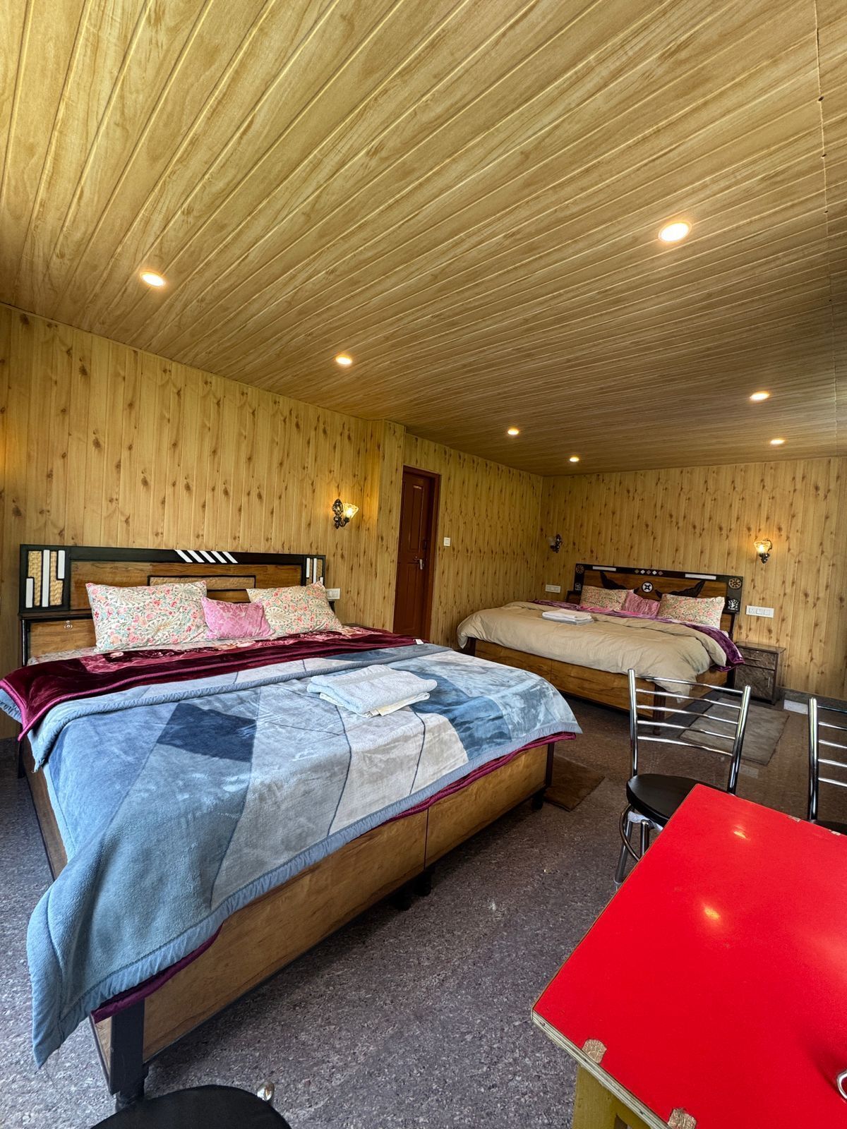 Quarto com duas camas, paredes de madeira e uma mesa vermelha.