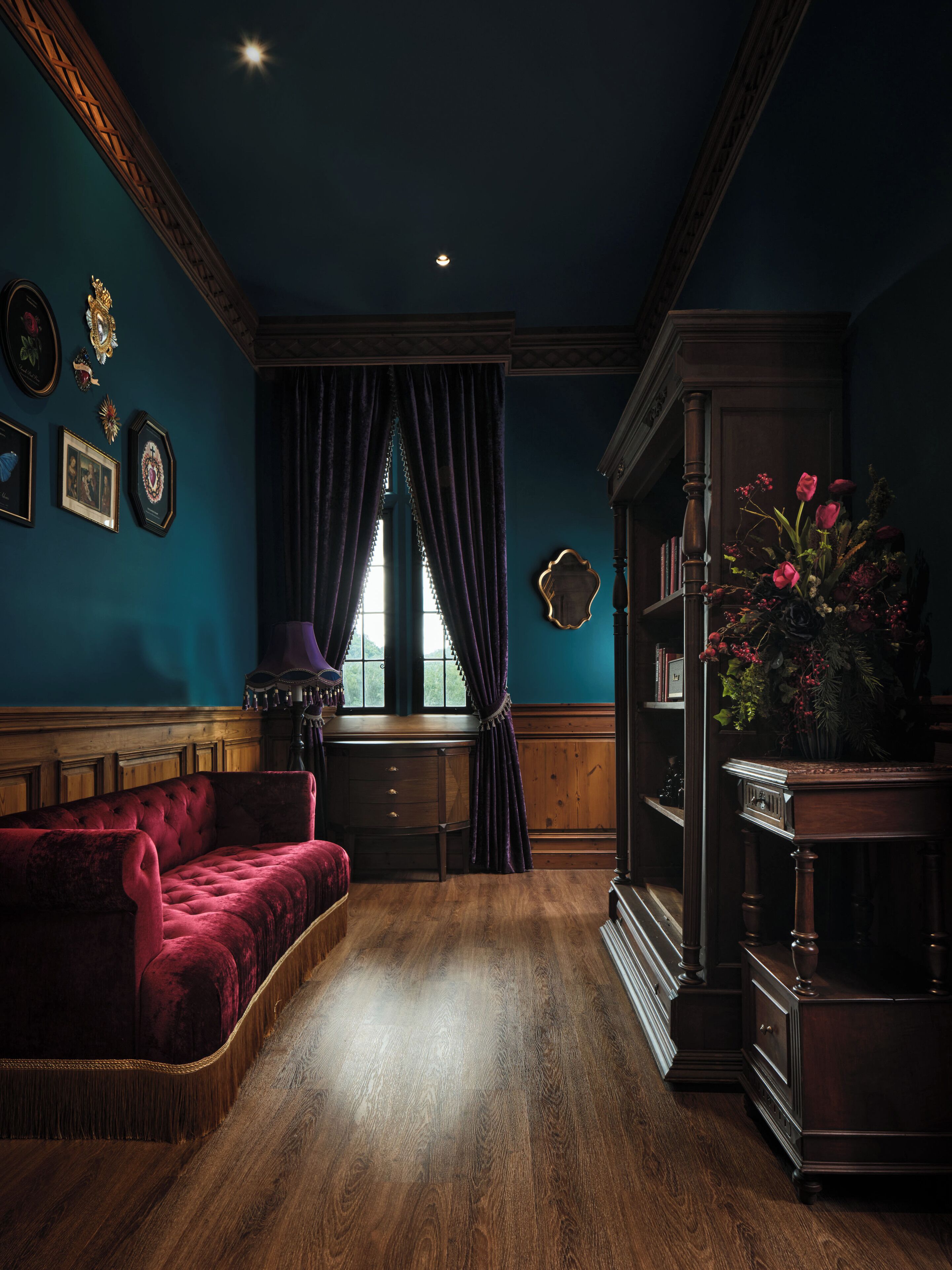 Um quarto com sofá de veludo vermelho, escrivaninha de madeira, estante de livros e janela com cortinas.