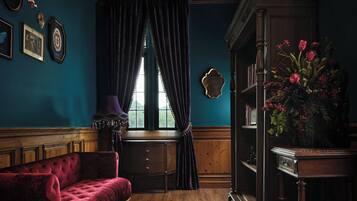 Um quarto com sofá de veludo vermelho, escrivaninha de madeira, estante de livros e janela com cortinas.