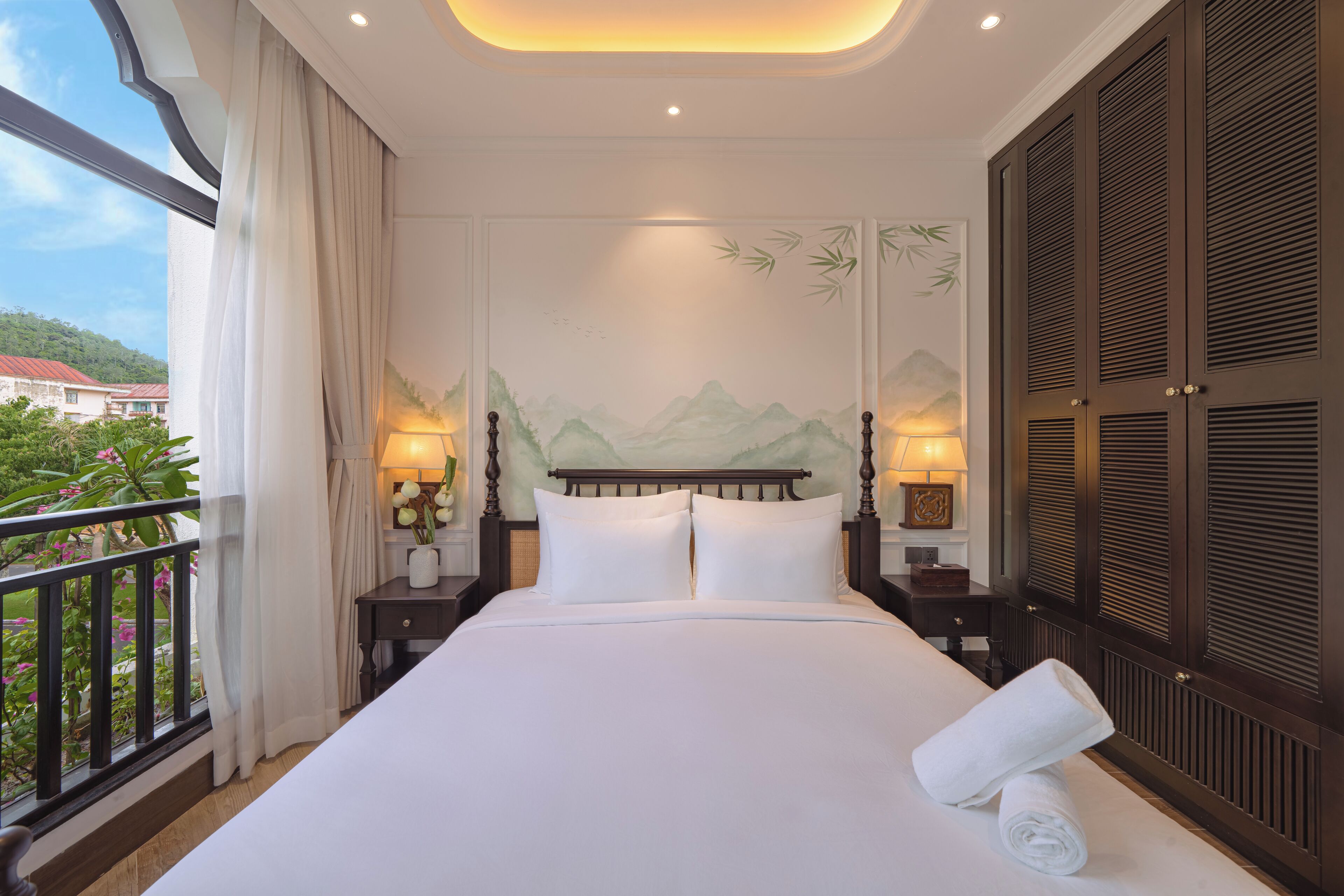 Quarto de hotel com cama, duas mesas de cabeceira, cortinas e vista para o verde lá fora.