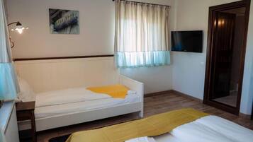 Quarto com cama, mesa de cabeceira, abajur, televisão na parede e janela com cortinas.