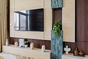 Uma sala de estar moderna com uma TV de tela plana fixada em uma parede de madeira, uma mesa de console com objetos decorativos e uma planta grande.