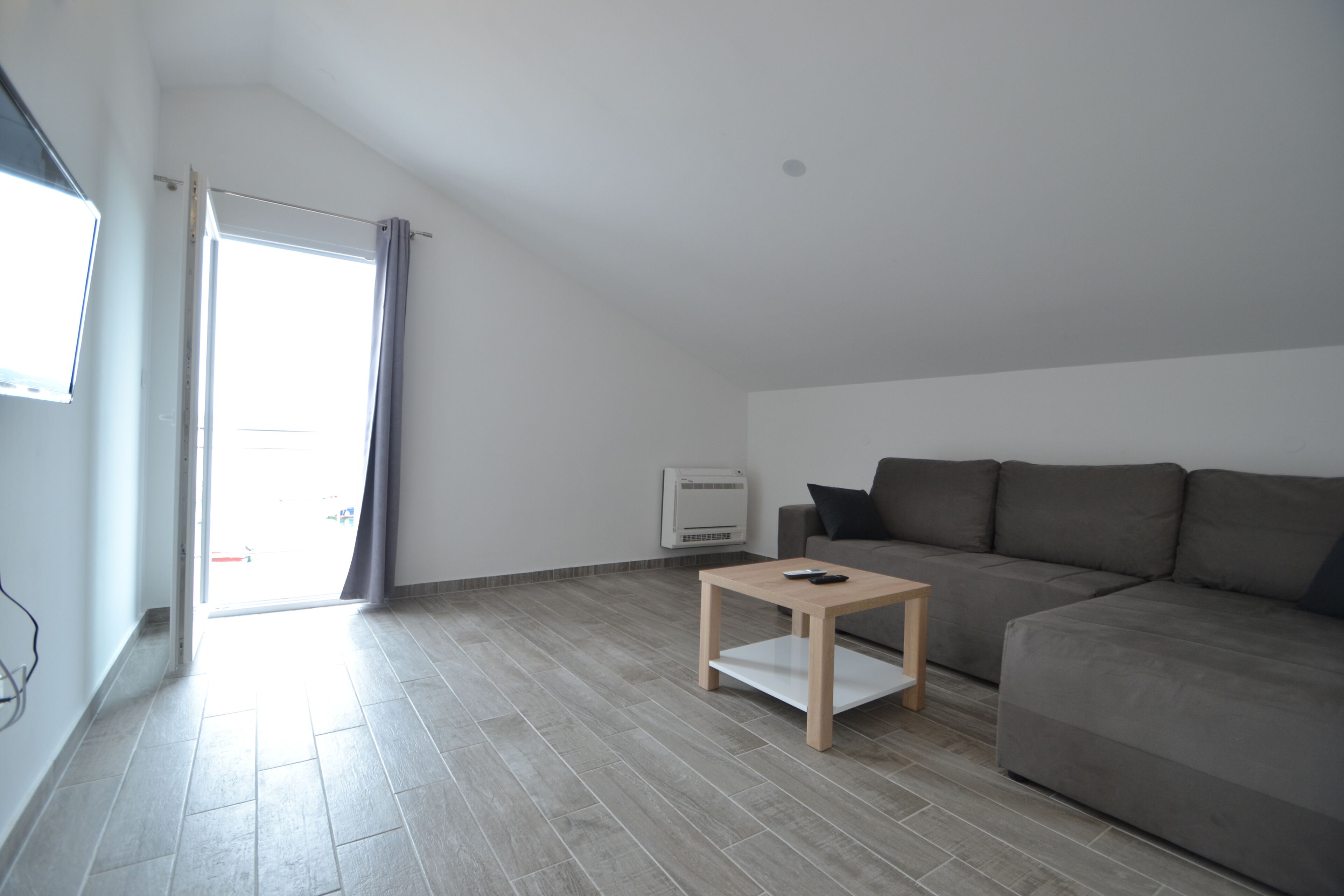 Uma sala de estar moderna com um sofá cinzento, uma mesa de madeira pequena e um ventilador de teto.