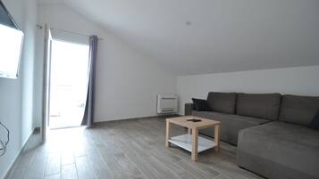 Uma sala de estar moderna com um sofá cinzento, uma mesa de madeira pequena e um ventilador de teto.