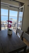 Uma área de refeições com mesa, cadeiras e vista para o mar e barcos.