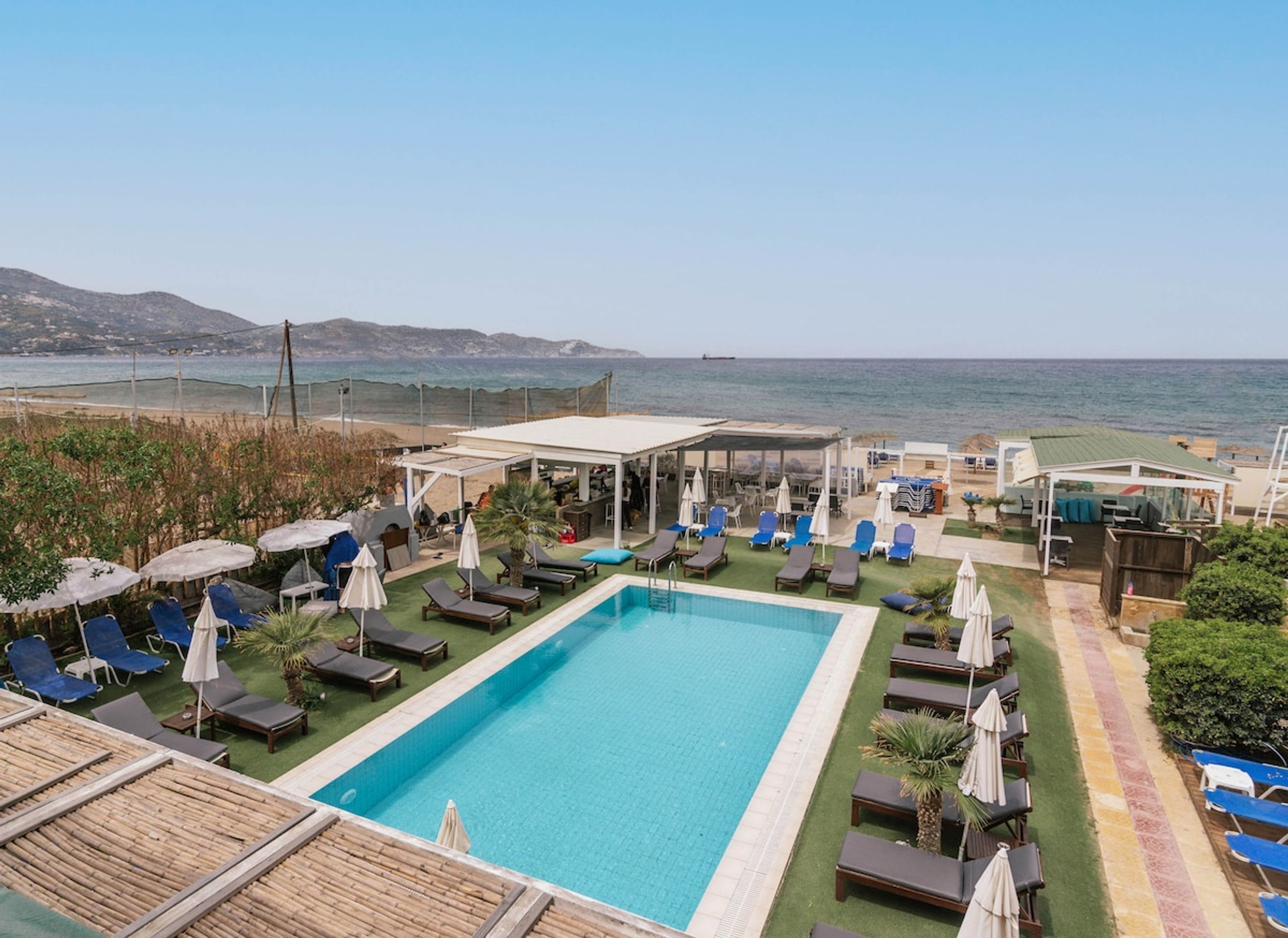 Piscina no terraço com espreguiçadeiras e guarda-sóis, com vista para uma praia e o mar.