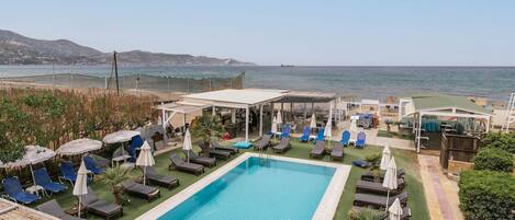 Piscina no terraço com espreguiçadeiras e guarda-sóis, com vista para uma praia e o mar.