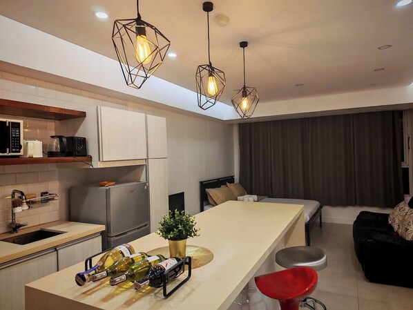 Cozinha moderna com ilha central, área de jantar com sofá e uma cama no quarto adjacente.