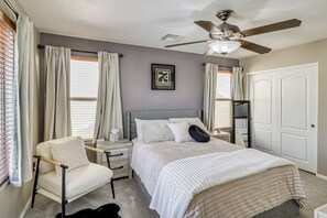 Quarto com cama, mesa de cabeceira, cadeira, ventilador de teto e porta.