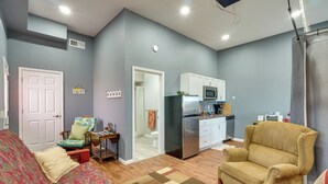 Sala de estar com sofá, poltrona e uma mesinha de centro com abajur. Há uma área de cozinha com geladeira e micro-ondas.