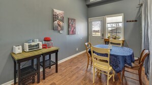 Espaço de refeições com mesa e cadeiras, micro-ondas, torradeira e uma pequena mesa com um recipiente vermelho.