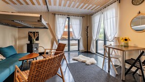 Quarto moderno com sofá, cadeiras, mesa, luminária pendente, porta-roupas e janela com cortinas.