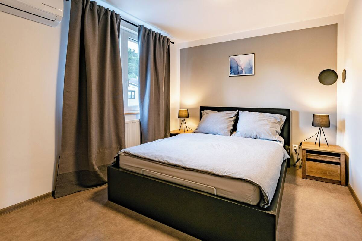 Quarto com cama, duas mesas de cabeceira, um quadro na parede e janela com cortinas.