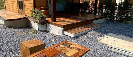 Uma casa moderna com fachada de madeira, varanda coberta e um pátio de cascalho com mesa e banquetas de madeira.