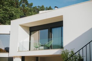 Um edifício moderno com varanda, grandes janelas e vista desobstruída para as árvores ao redor.