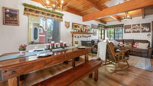 Um interior rústico com uma mesa de jantar de madeira, bancos, uma cadeira de balanço e um espaço de estar aconchegante.