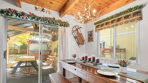 Uma mesa de jantar de madeira com bancos, um candelabro e uma porta de vidro que dá para uma área externa.