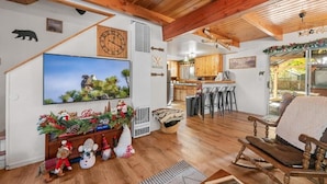 Um ambiente acolhedor com teto de madeira, TV na parede, cozinha e área de estar com uma poltrona de balanço.