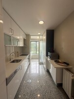 Uma cozinha moderna com uma pia de aço inoxidável, armários brancos, um micro-ondas e vista para uma varanda através de uma porta de vidro.