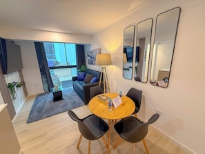 Uma sala de estar moderna com uma mesa redonda de madeira, cadeiras pretas, um sofá e uma janela grande.