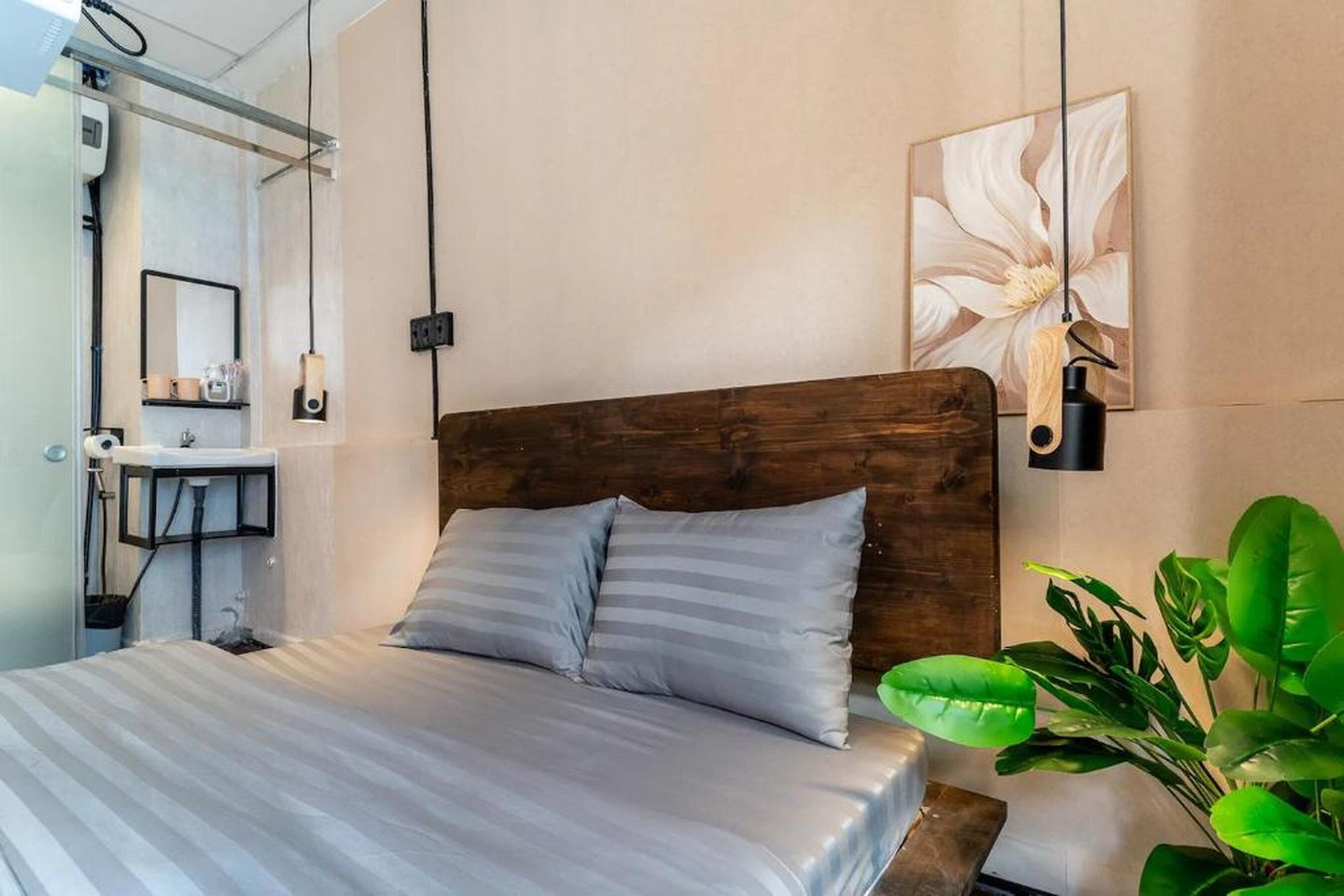 Quarto com cabeceira de madeira, cama com roupa de cama listrada, mesa de cabeceira, espelho e luminária fixada na parede.