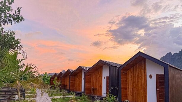 Uma fileira de cabanas de madeira com um caminho que as leva, cercada por vegetação.