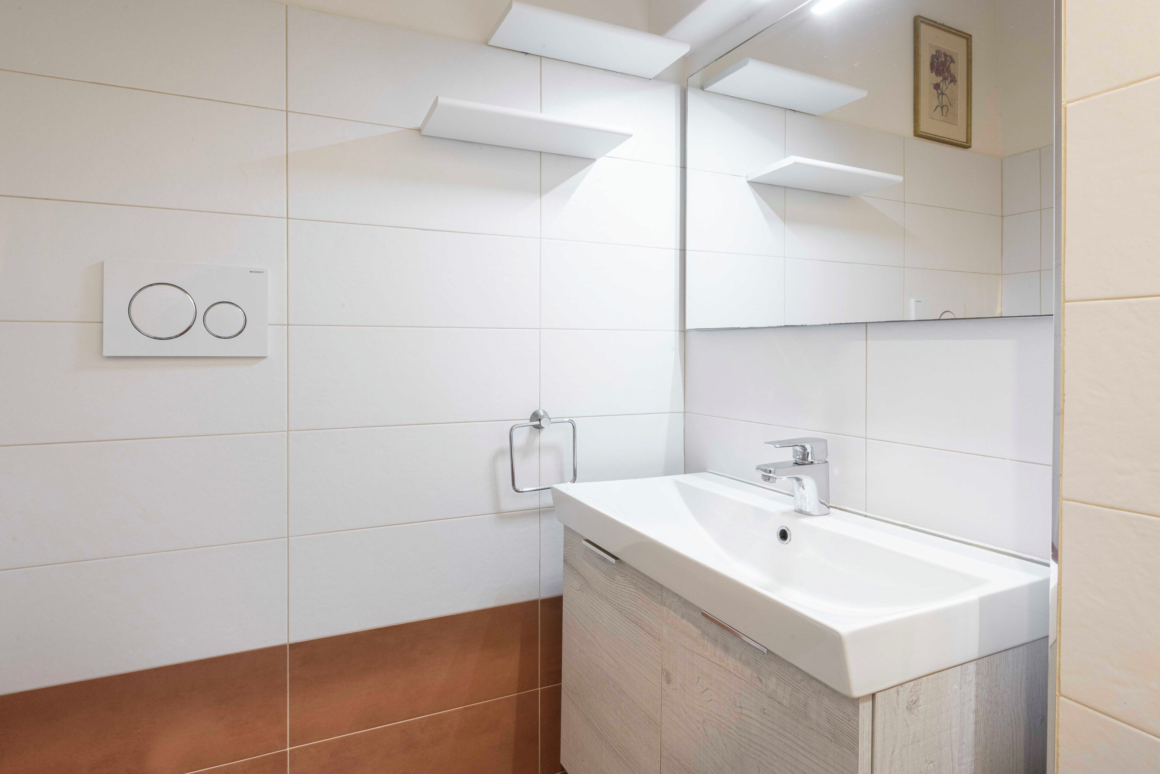 Um banheiro moderno com azulejos brancos, pia branca e espelho.