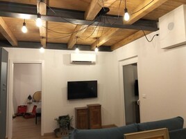 Uma sala de estar com televisão de tela plana, vigas de madeira no teto e um sofá azul.
