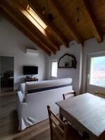 Quarto com teto de madeira, um sofá, uma TV, uma mesa de jantar e uma janela.