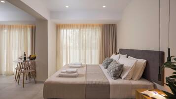 Quarto de hotel com cama, mesa de cabeceira, cortinas e área de refeições com cadeiras e uma mesa.