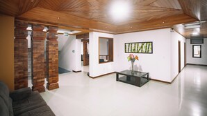 Um hall espaçoso com teto de madeira, uma mesa de centro de vidro com flores e uma placa indicando 'Next'.