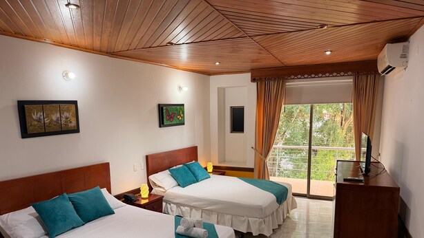 Quarto de hotel com duas camas, teto de madeira, varanda com vista e uma mesa de trabalho com televisão.