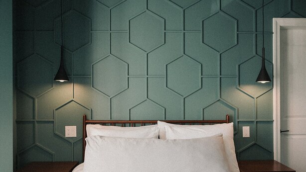 Quarto com cama, duas luminárias de cabeceira e uma parede com padrão geométrico.